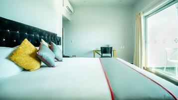 Quarto de hotel moderno com uma cama grande, televisão de tela plana, uma mesinha e uma janela com cortinas.