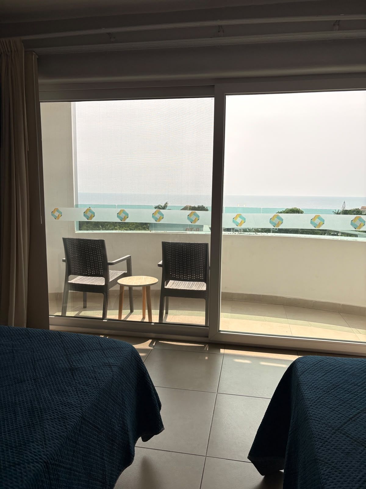 Uma varanda com vista para o mar, duas cadeiras e uma mesa.