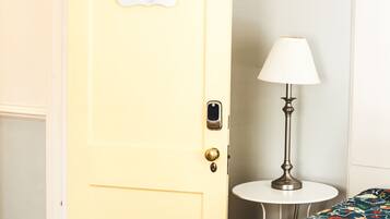 Um quarto com uma porta identificada como "MAGNOLIA", uma mesa redonda com uma luminária e uma cama com colcha florida.