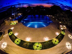 Área de piscina circular ao ar livre, com um elemento aquático central, cercada por um muro baixo com luzes espaçadas regularmente.