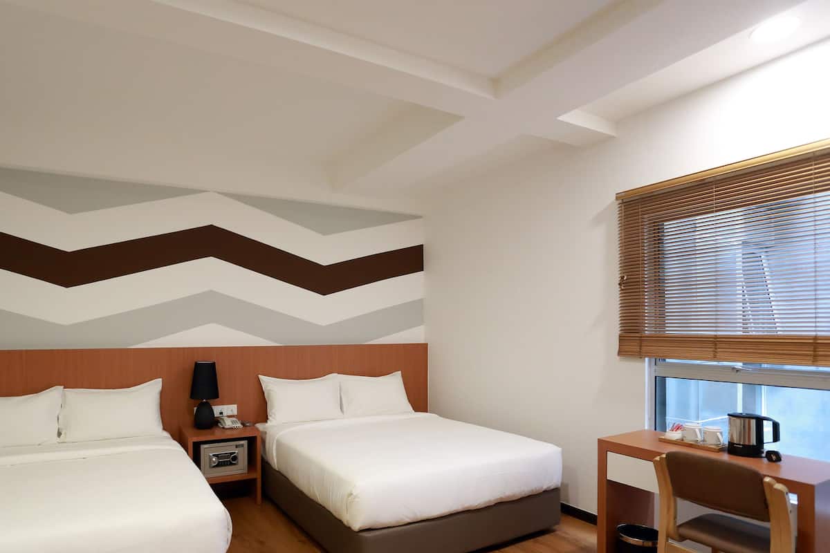 Quarto de hotel com duas camas, uma mesa, uma cadeira, cafeteira e janela com persianas.