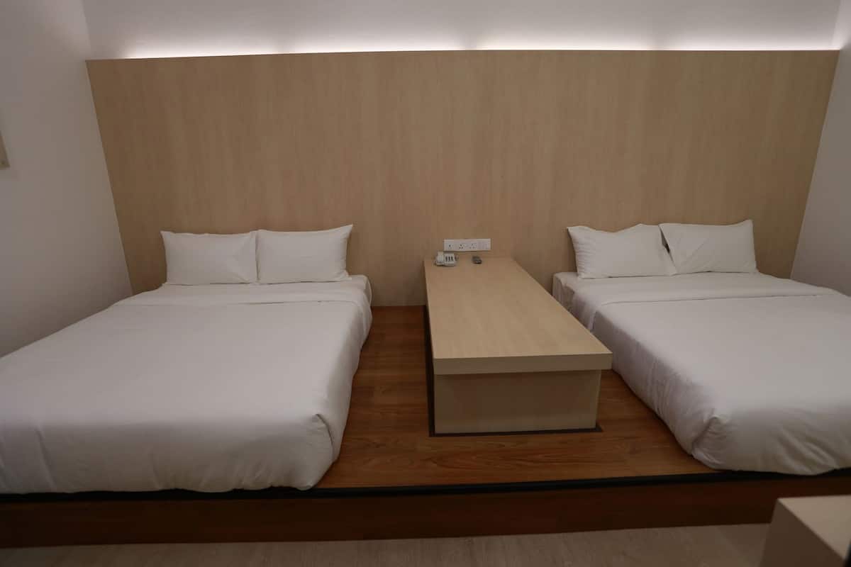Quarto de hotel com duas camas de solteiro, uma mesa central e cabeceira de madeira.