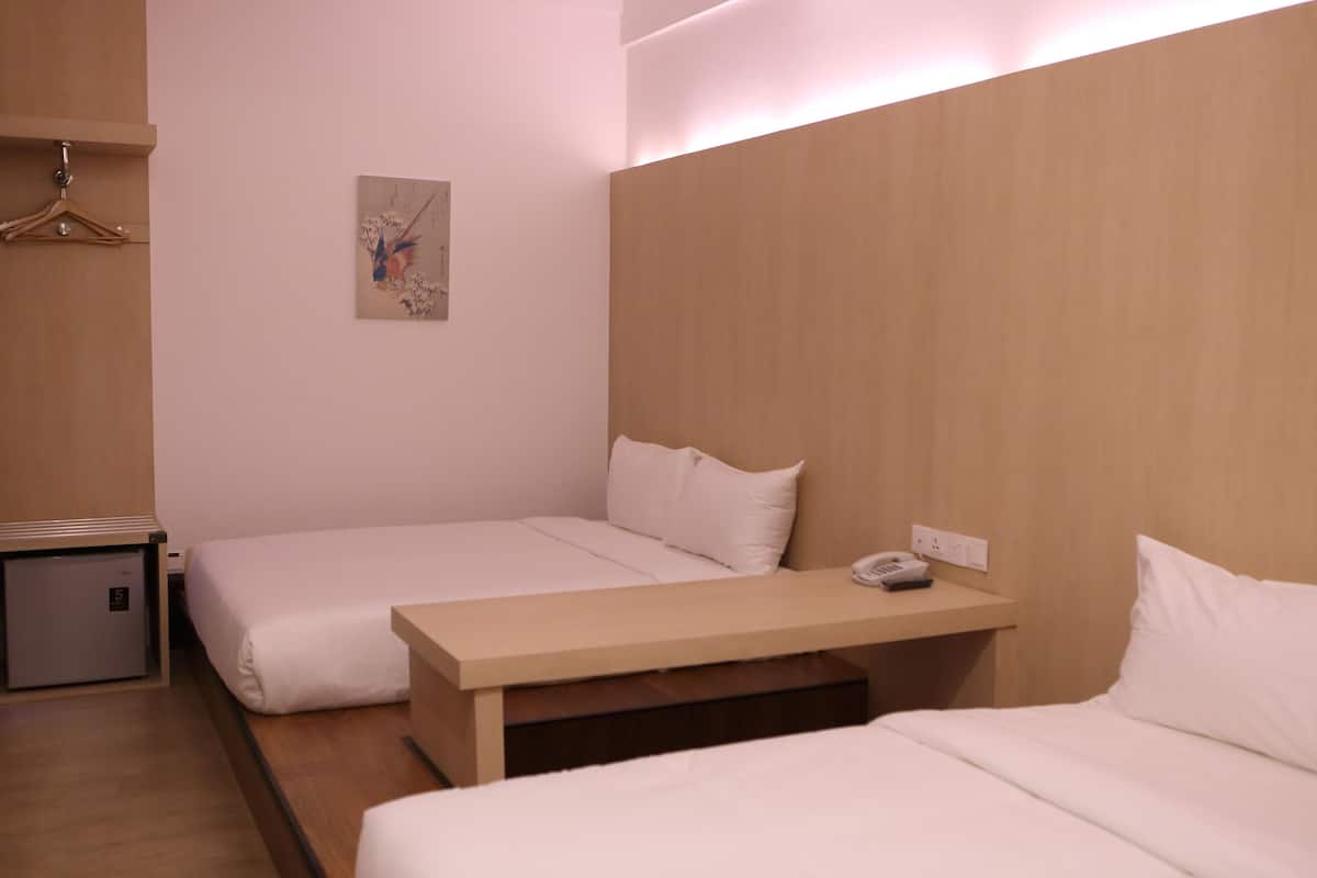 Quarto de hotel com duas camas de solteiro, uma pequena mesa de trabalho, telefone e uma obra de arte na parede.