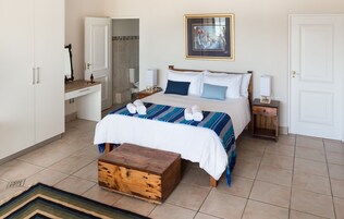 Quarto de hotel bem arrumado com uma cama grande, mesas de cabeceira, um baú de madeira e um quadro na parede.