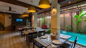Um restaurante com mesas ao ar livre, piscina e tela de televisão.