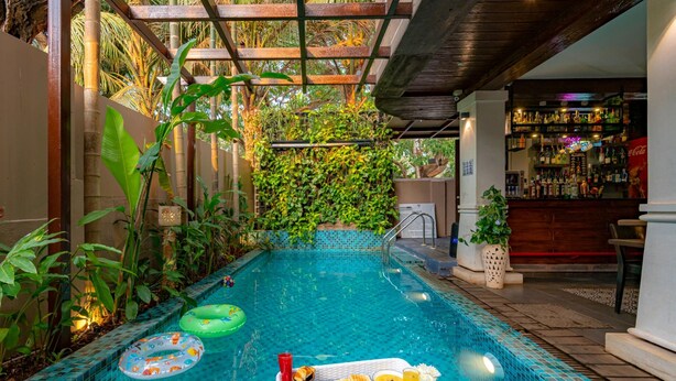 Piscina com borda azulejada, rodeada por plantas e área de bar com vários frascos.