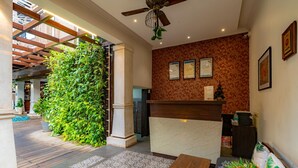 Uma área de recepção com um balcão de madeira, parede com quadros de certificados e um jardim vertical verde.
