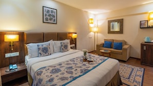 Quarto de hotel com cama, mesa de cabeceira, abajur e um pequeno sofá.