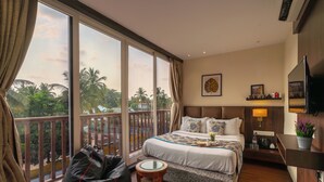 Quarto de hotel com uma varanda ampla, cama com cabeceira decorativa, mesa redonda pequena e televisão fixada na parede.