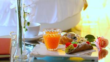 Mesa de café da manhã com um vaso de flores brancas, um copo de suco de laranja, doces e uma rosa.