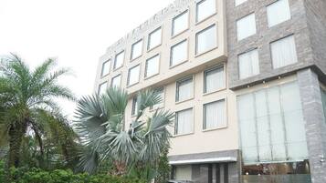 Um hotel com vários andares, fachada moderna, amplas janelas e estacionamento com um carro.