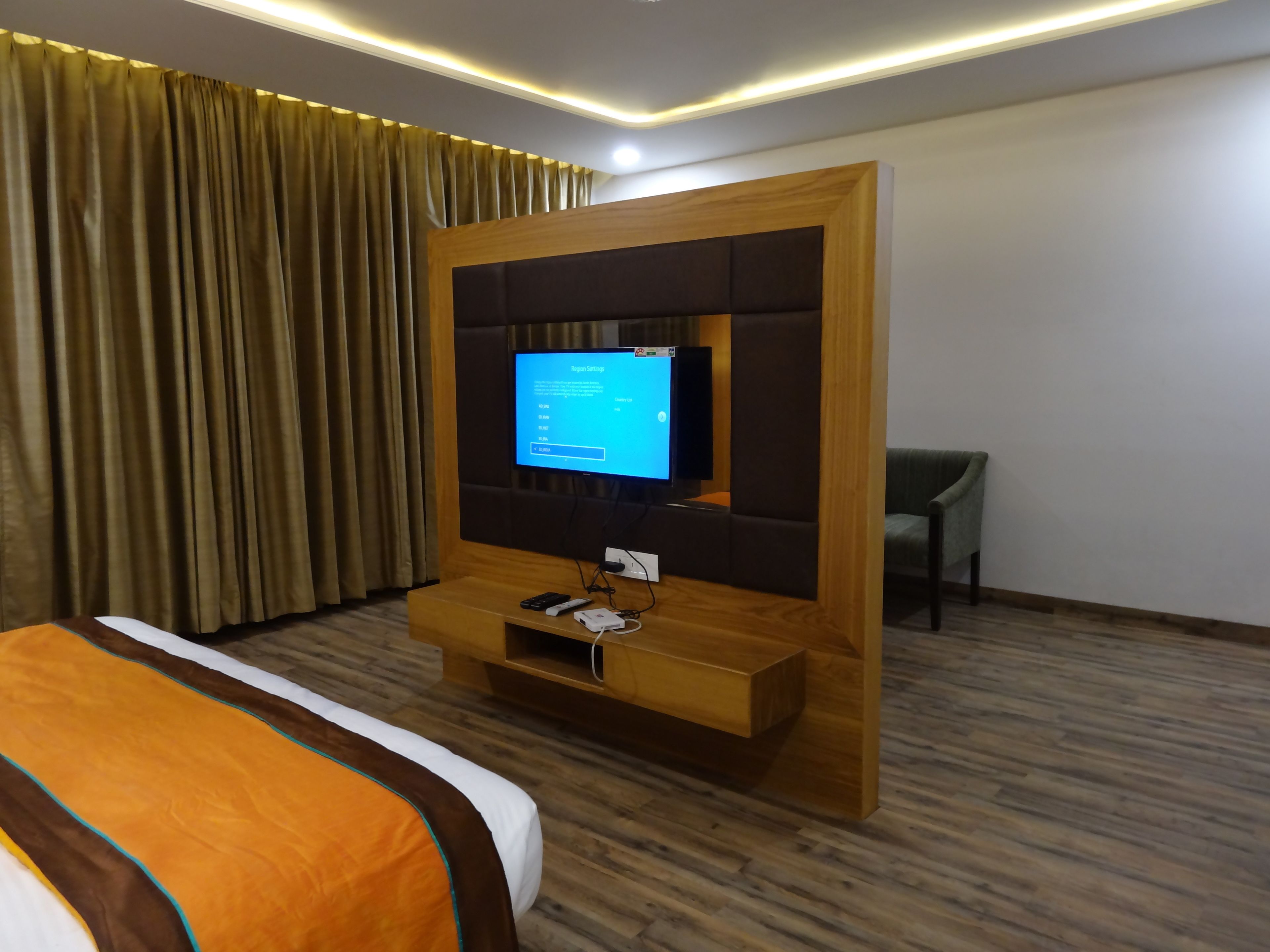 Quarto de hotel com uma cama grande, um suporte de madeira para televisão com uma TV de tela plana, uma escrivaninha e uma cadeira.