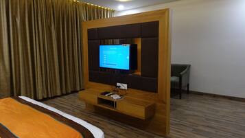 Quarto de hotel com uma cama grande, um suporte de madeira para televisão com uma TV de tela plana, uma escrivaninha e uma cadeira.