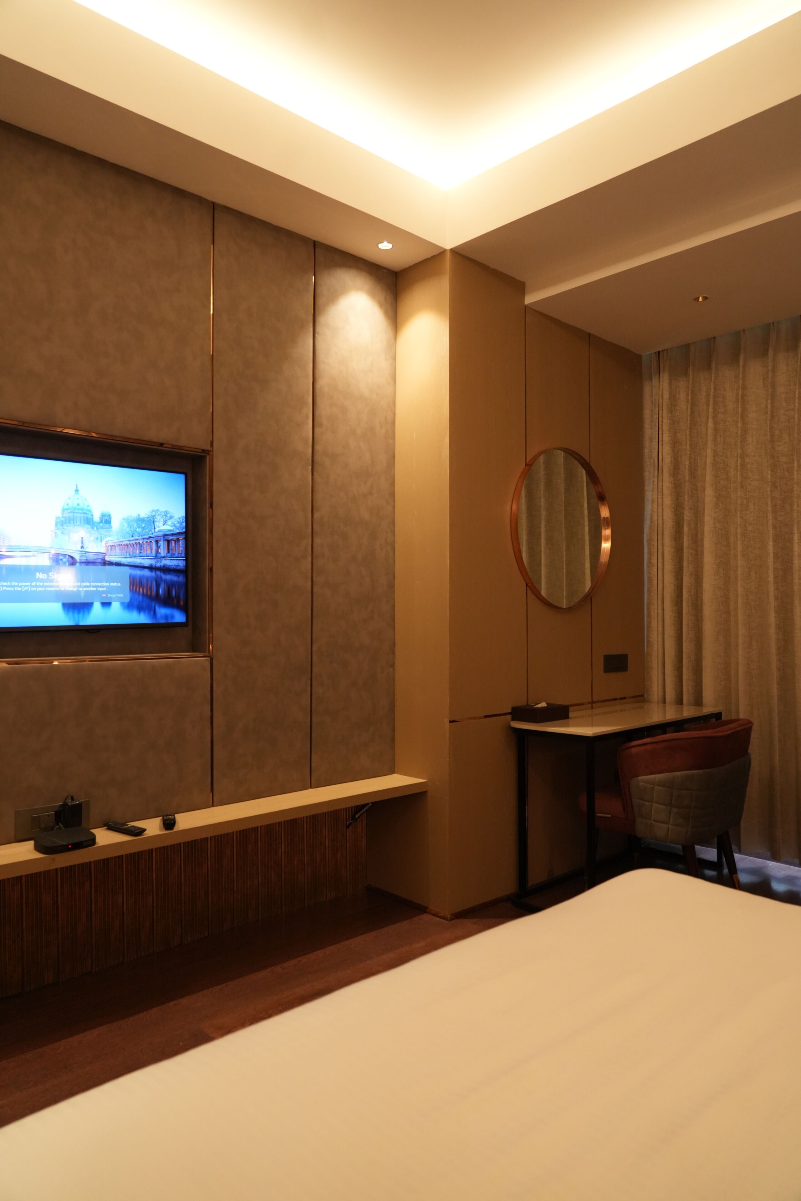 Quarto de hotel com uma cama grande, televisão de tela plana na parede, uma mesinha e uma cadeira.