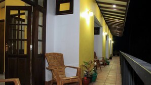 Um corredor com cadeiras, plantas em vasos, uma porta de madeira e piso de azulejos.