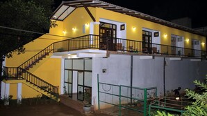 Um edifício de dois andares com fachada amarela, uma varanda no andar superior e uma escadaria que leva à entrada.