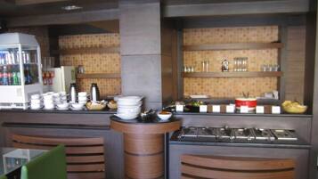 Buffet montado com diversas estações de serviço, um refrigerador com bebidas e uma variedade de pratos expostos em prateleiras.