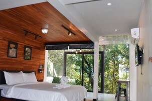 Quarto moderno com teto de madeira, uma cama grande, uma mesa pequena e vista para o verde lá fora.