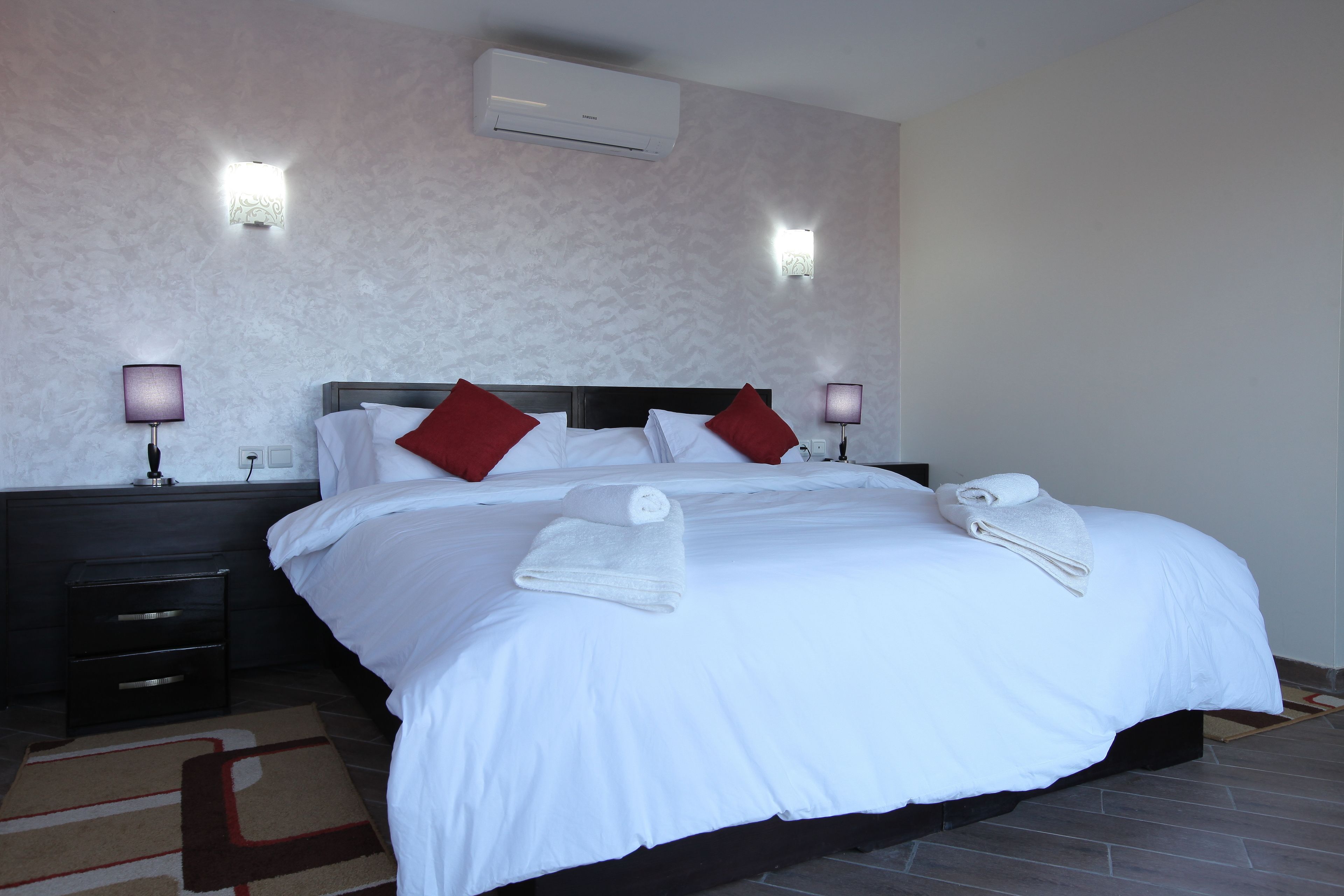Quarto de hotel com uma cama grande, duas mesas de cabeceira com luminárias, ar condicionado fixado na parede e um tapete estampado.