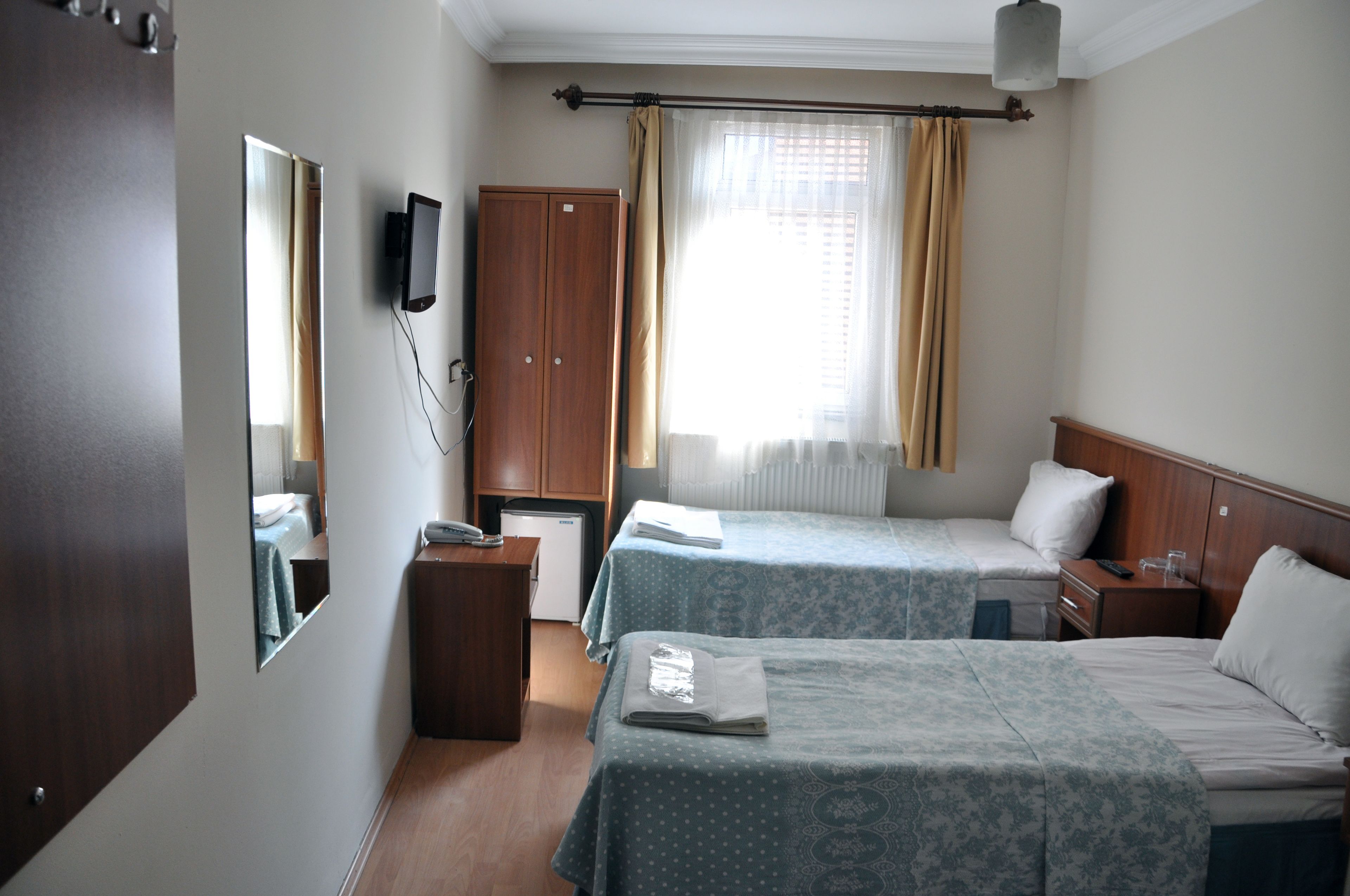 Quarto de hotel com duas camas, guarda-roupa, escrivaninha, cadeira, televisão e janela com cortinas.