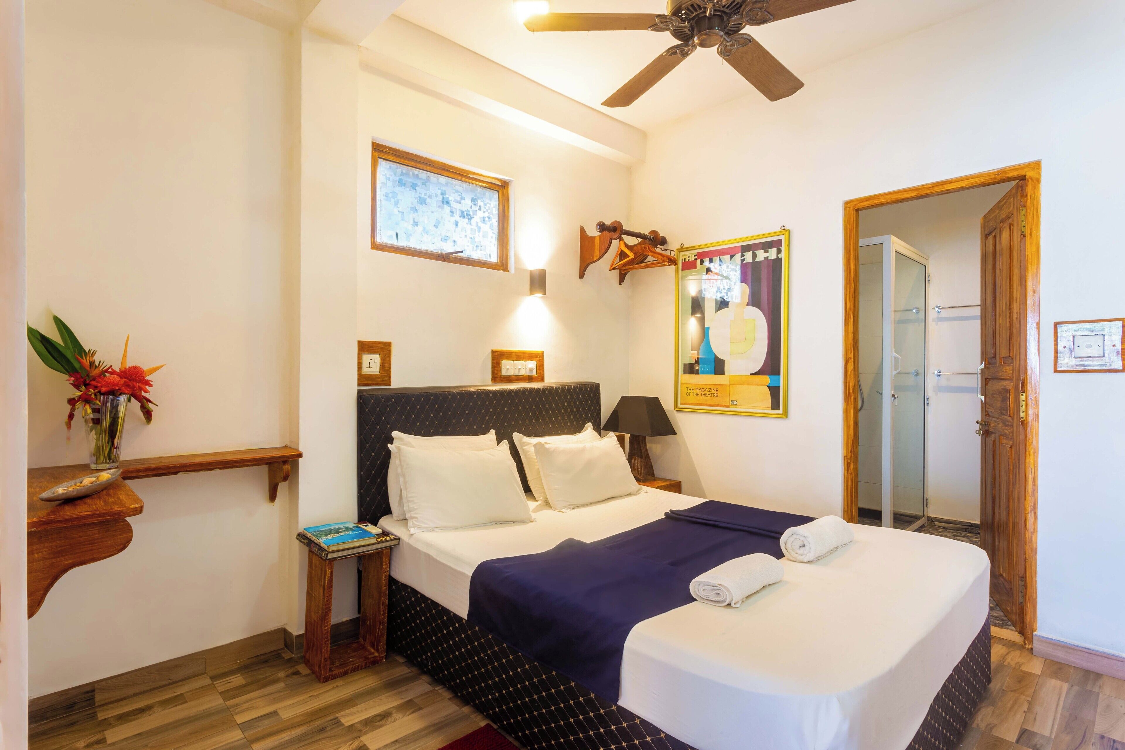 Quarto de hotel com cama, mesa de cabeceira, abajur e ventoinha no teto.