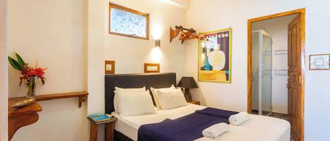 Quarto de hotel com cama, mesa de cabeceira, abajur e ventoinha no teto.