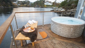 Um terraço com hidromassagem, uma mesa de madeira com toalhas e comida, e vista para um rio e casas.