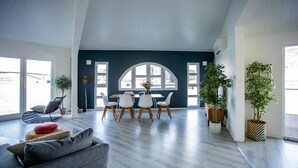 Uma sala de estar ampla com pé direito alto, uma mesa de jantar com cadeiras e grandes janelas que proporcionam luz natural.