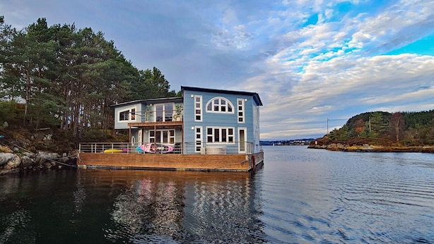 Uma casa à beira-mar com deck de madeira, janelas amplas e um píer.