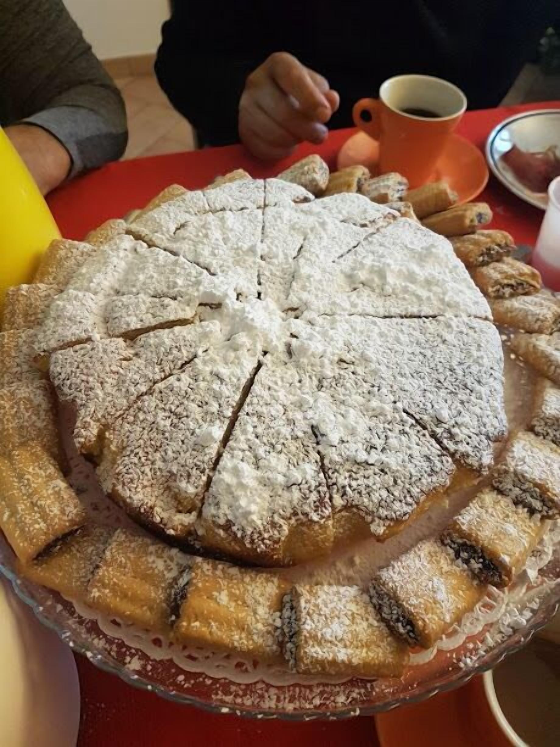 Um bolo redondo coberto com açúcar em pó, colocado sobre um prato de vidro para servir.