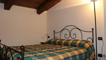 Quarto com cama, mesa de cabeceira, abajur e vigamento de madeira no teto.