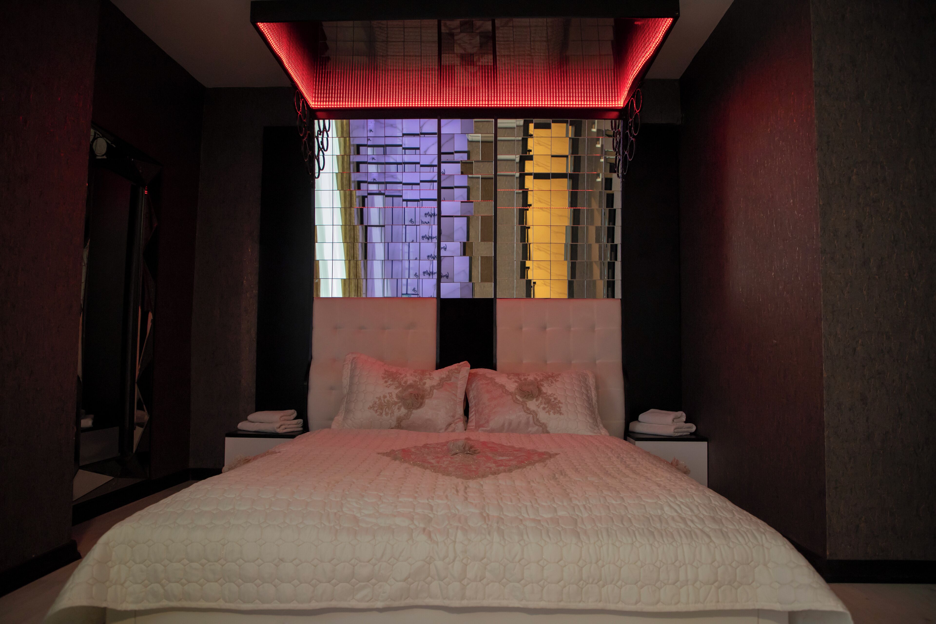 Quarto moderno com uma cama grande, cabeceira com design único e uma faixa de luz vermelha acima da cama.