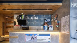 Uma área de recepção com teto de madeira, balcão de atendimento, televisão na parede e um cartaz divulgando um programa esportivo.