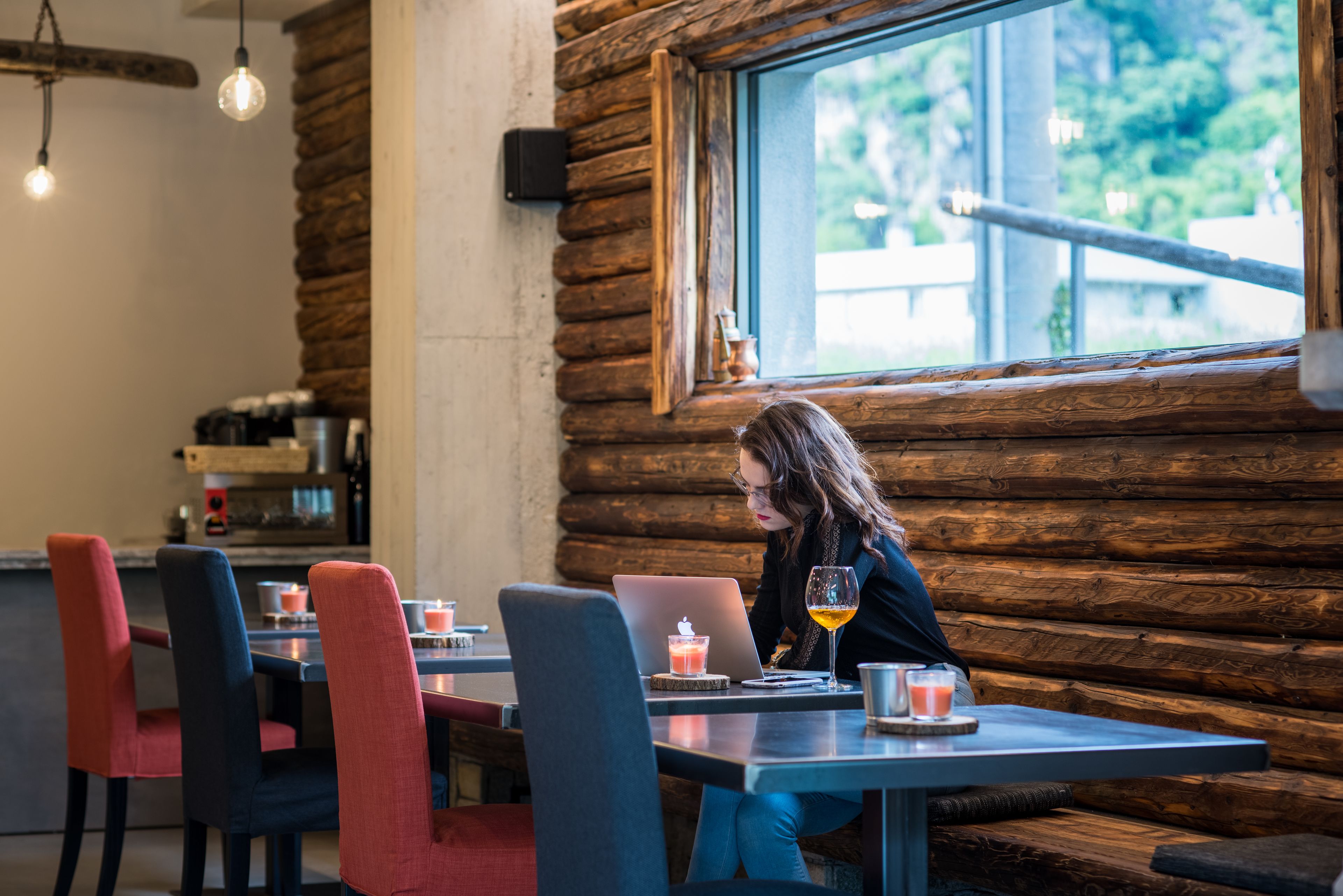 Interior acolhedor estilo cabana, com paredes de madeira, uma janela grande e uma mesa com um laptop e um copo de vinho.