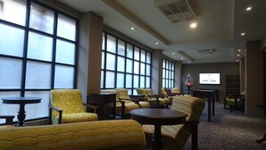 Um saguão de hotel com grandes janelas, várias áreas de estar e uma tela de projeção exibindo 'nite & day'.