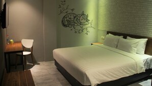 Um quarto com uma cama, uma cadeira, uma mesa pequena e um ornamento na parede.