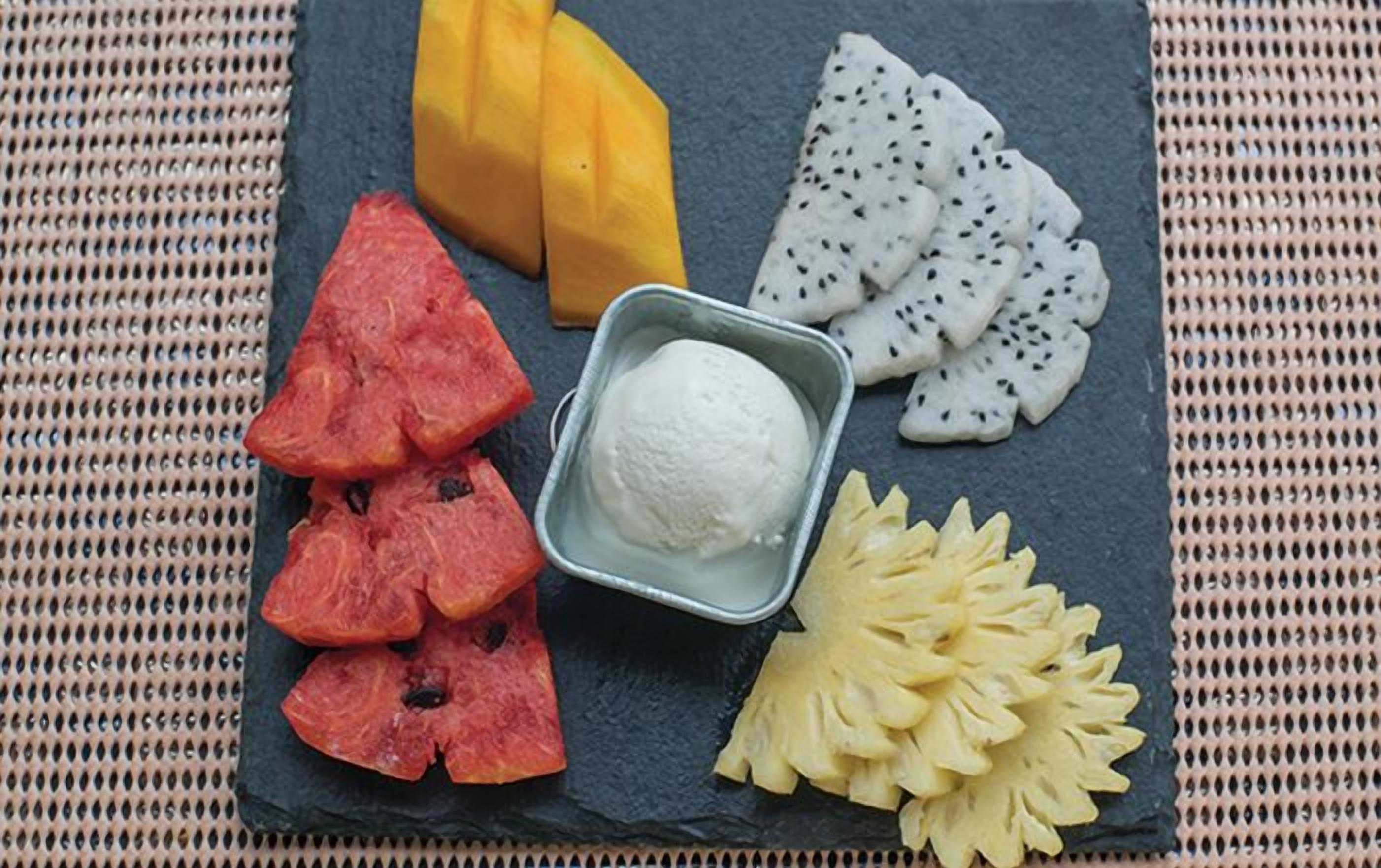 Uma lousa de ardósia preta com melancia, pitaya e abacaxi sobre um tapete tecido.