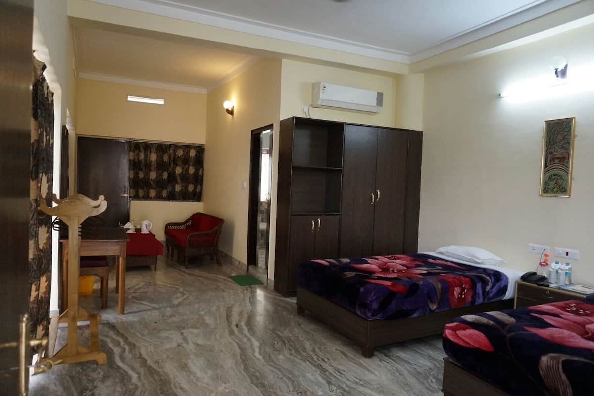 Quarto de hotel com cama, guarda-roupa, escrivaninha, duas cadeiras e ar condicionado.