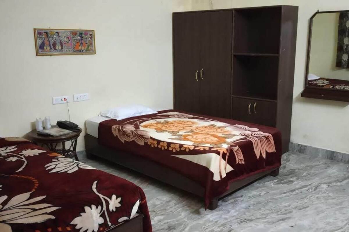 Quarto de hotel com duas camas, um guarda-roupa, uma mesinha com uma cadeira, um espelho fixado na parede e um quadro decorativo.