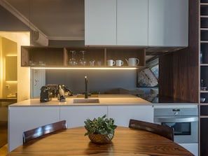 Cozinha moderna com armários brancos, forno embutido e área de refeições com mesa e cadeiras de madeira.