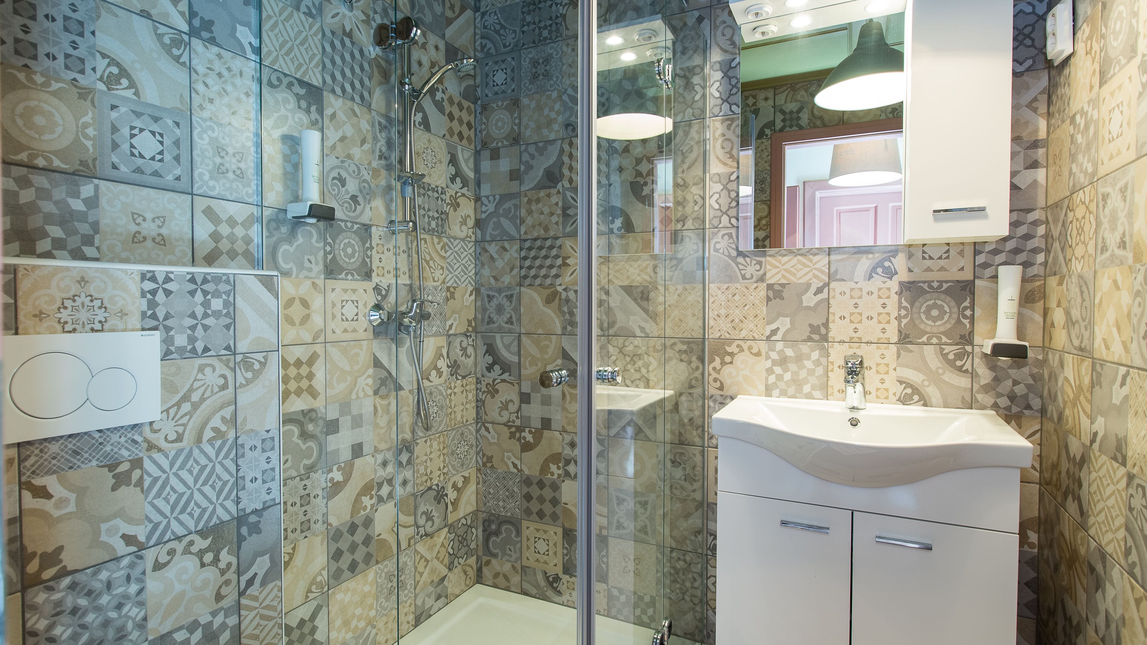 Casa de banho com azulejos estampados, cabine de duche em vidro, lavatório e espelho.