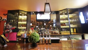 Uma área de bar com um bartender, prateleiras de copos e garrafas de bebidas alcoólicas.