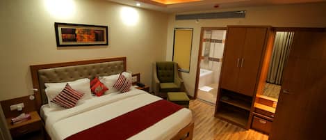 Quarto de hotel com uma cama grande, uma cadeira, um armário e área de chuveiro.