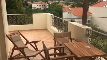 Uma varanda com mesa e cadeiras, piso de azulejos e vista para uma cidade montanhosa.