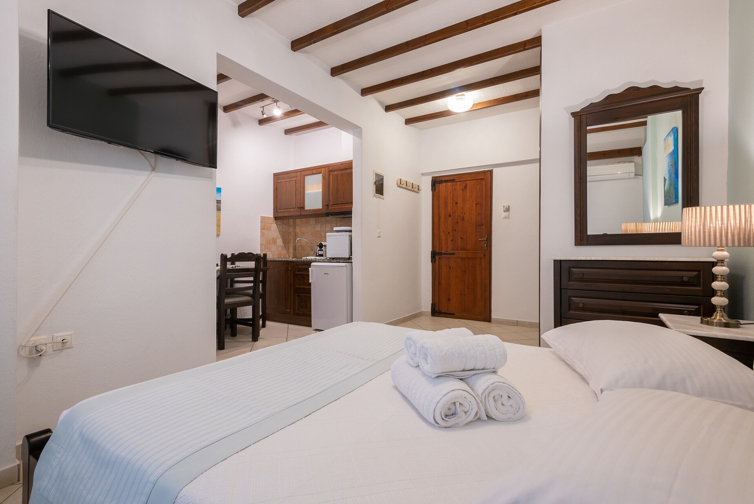 Quarto de hotel com cama, escrivaninha, cadeira, televisão e área de cozinha.