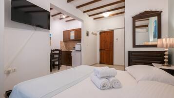 Quarto de hotel com cama, escrivaninha, cadeira, televisão e área de cozinha.
