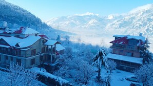 Uma aldeia coberta de neve com casas de madeira tradicionais, montanhas ao fundo e um céu limpo.
