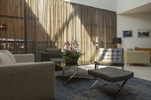 Uma sala de estar moderna com um sofá, poltrona, banquinho e uma mesa de centro de vidro com um arranjo de flores.