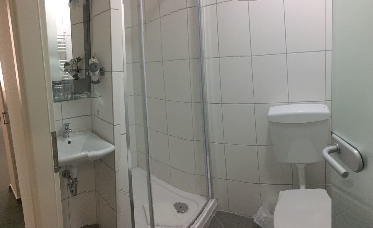 Casa de banho pequena com lavatório branco, sanita e cabine de duche em vidro.