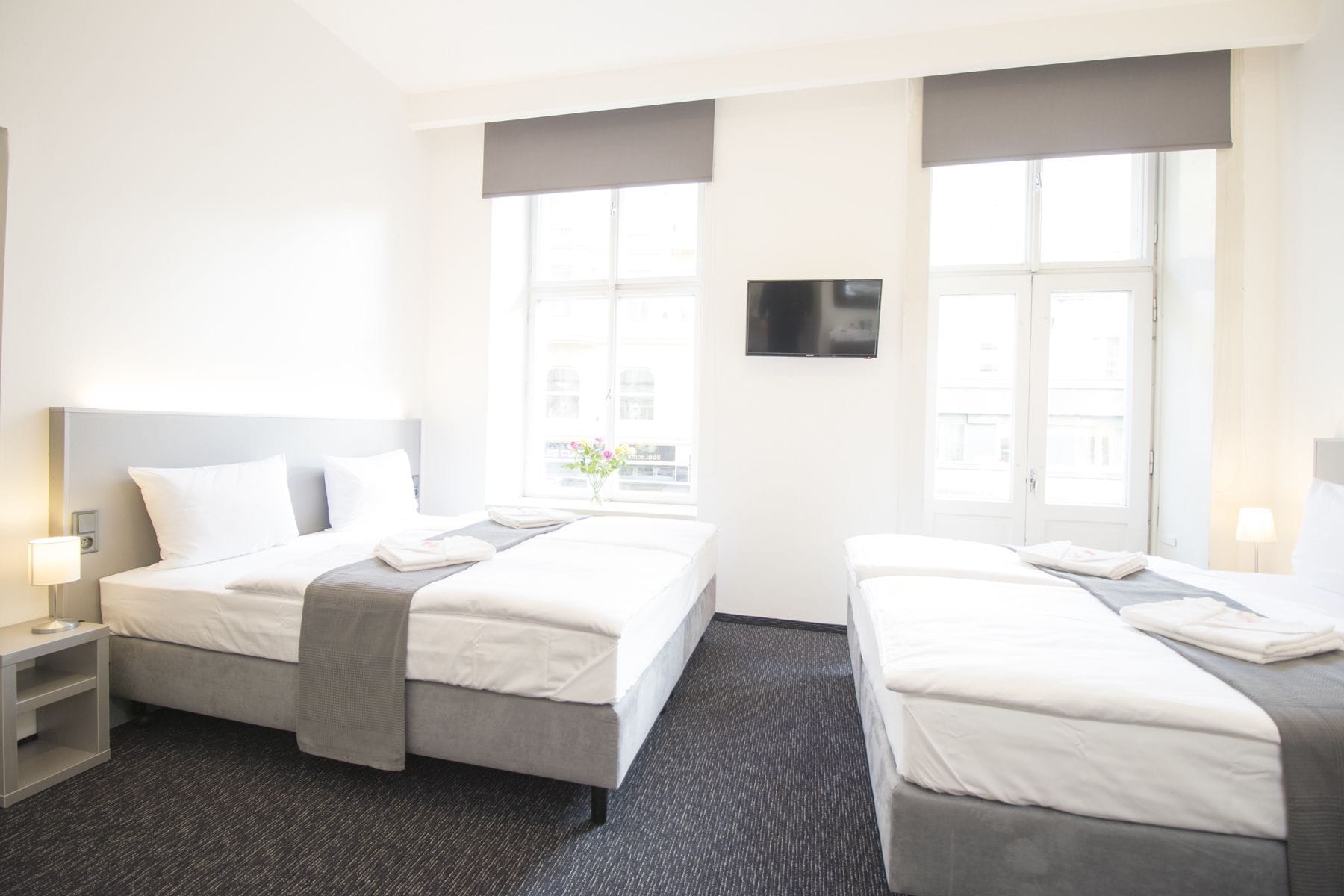 Quarto de hotel com duas camas, televisão e janela com vista para edifícios.